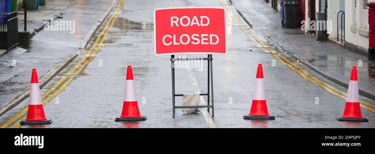 Road ahead closed sign with traffic cones and red barrier fence ...