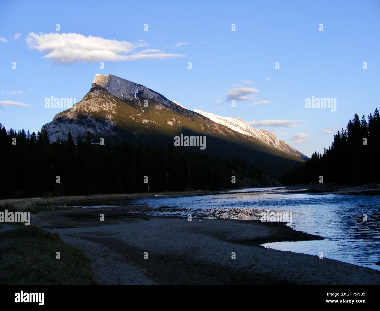 Mt. Rundle peak illuminated with light at sunset beside the Bow River ...