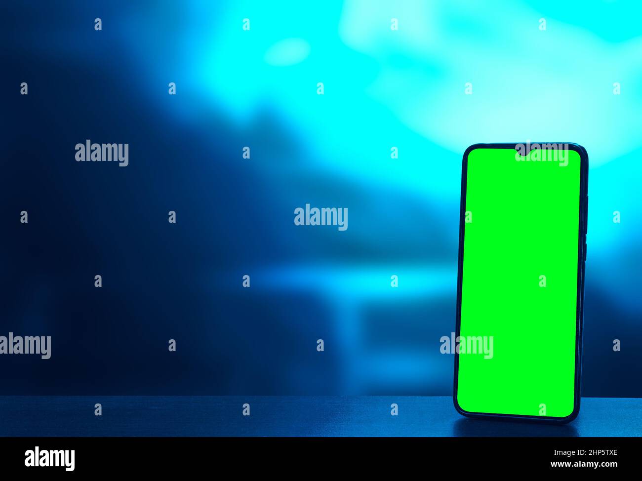 Closeup shot of a green screen on a mobile phone against a blue blurry ...