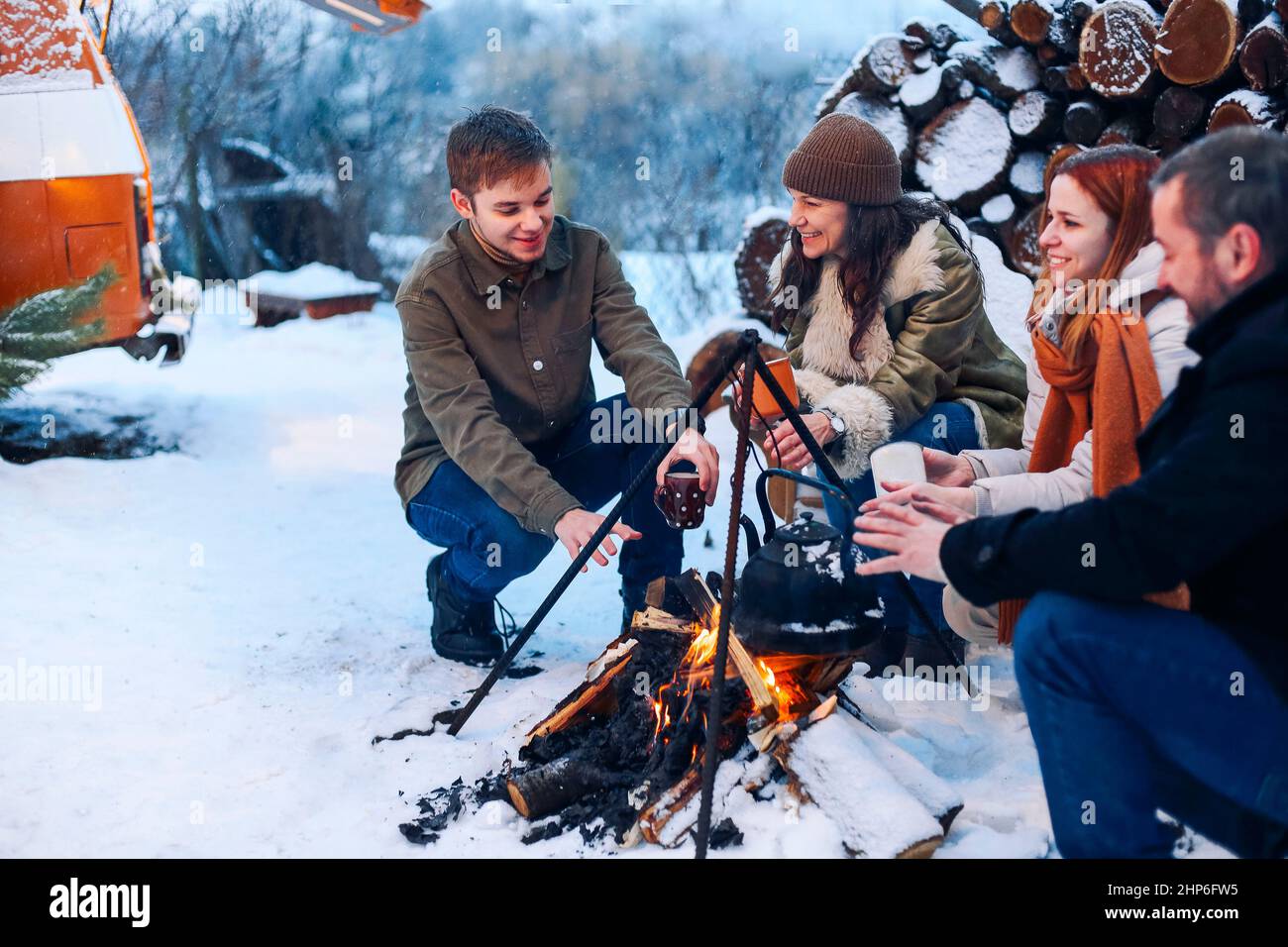 Group of friends gathering around bonfire in backyard, drinking tea and ...