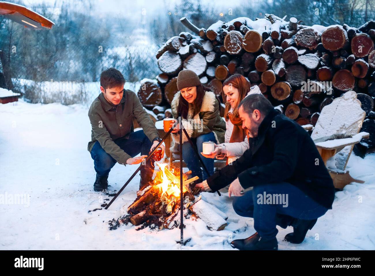 Group of friends gathering around bonfire in backyard, drinking tea and ...