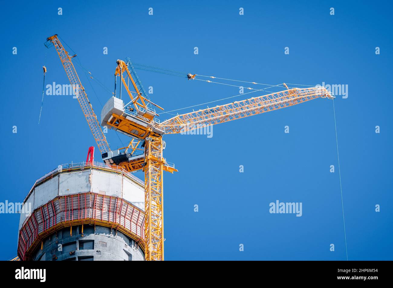 Two yellow cranes on top of a skyscraper under construction on a blue ...