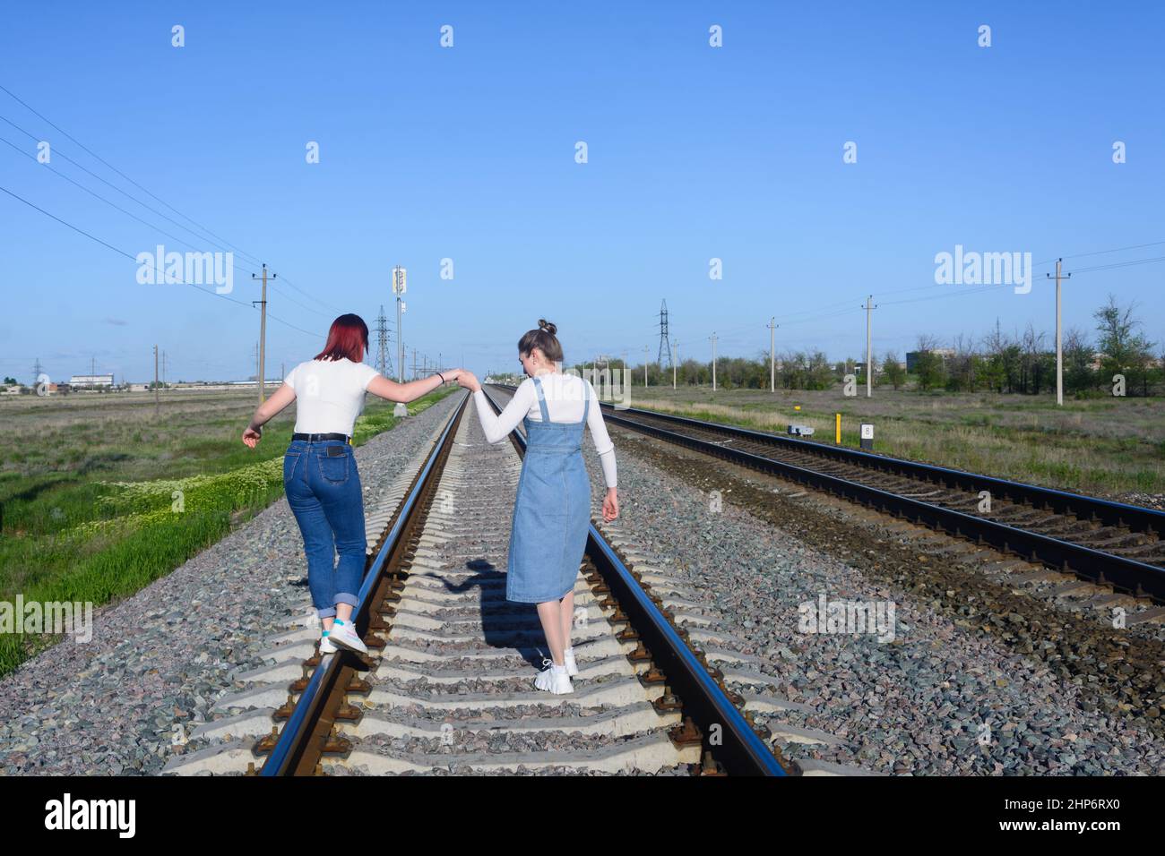 Teenage girl by hand with young woman walks on the rails of railway and ...