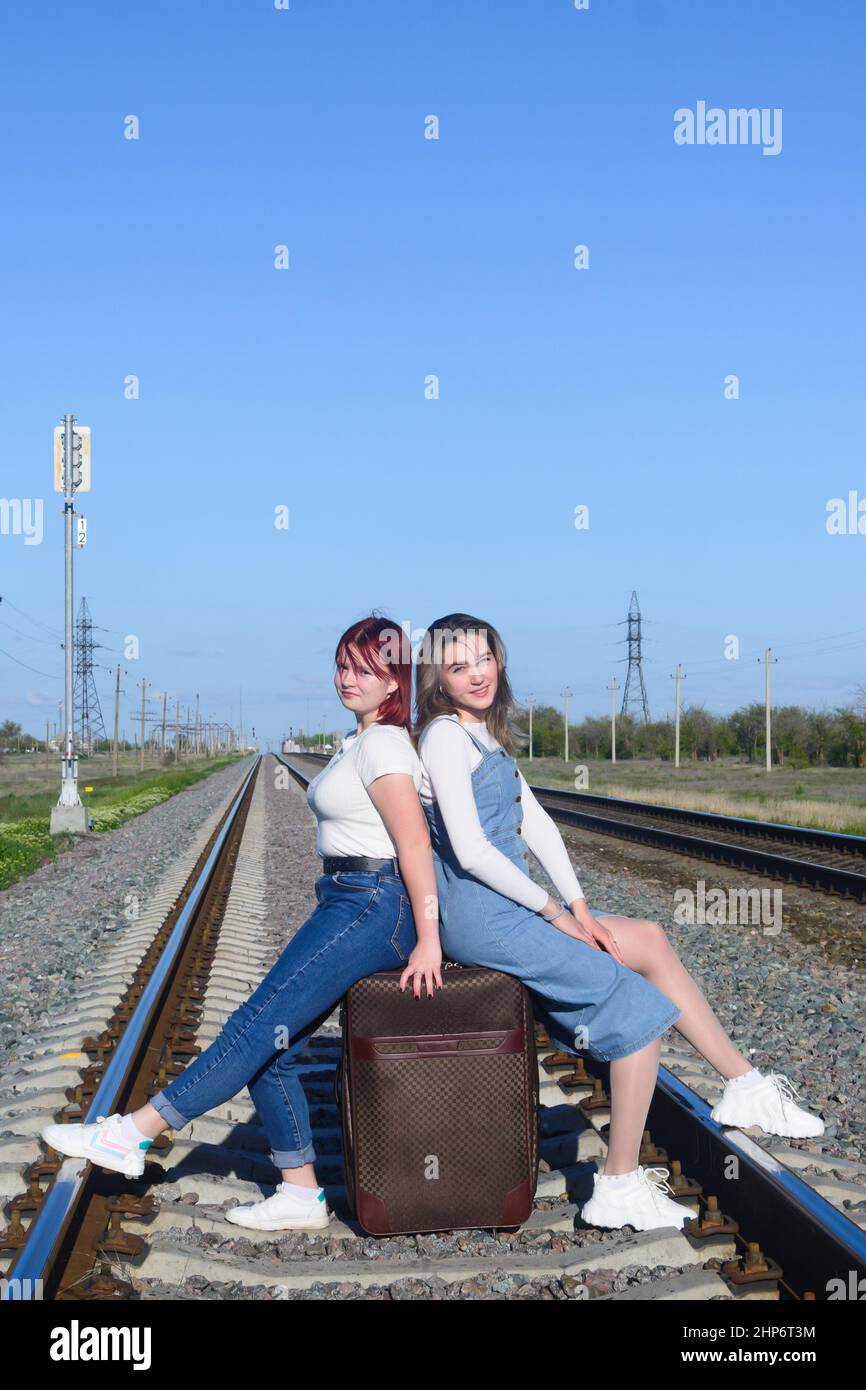 Two young women are sitting on large suitcase. Railroad rails on ...
