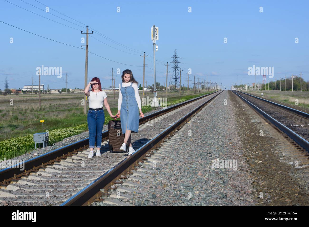 Beautiful young ladies are walking with suitcase on the railroad tracks ...
