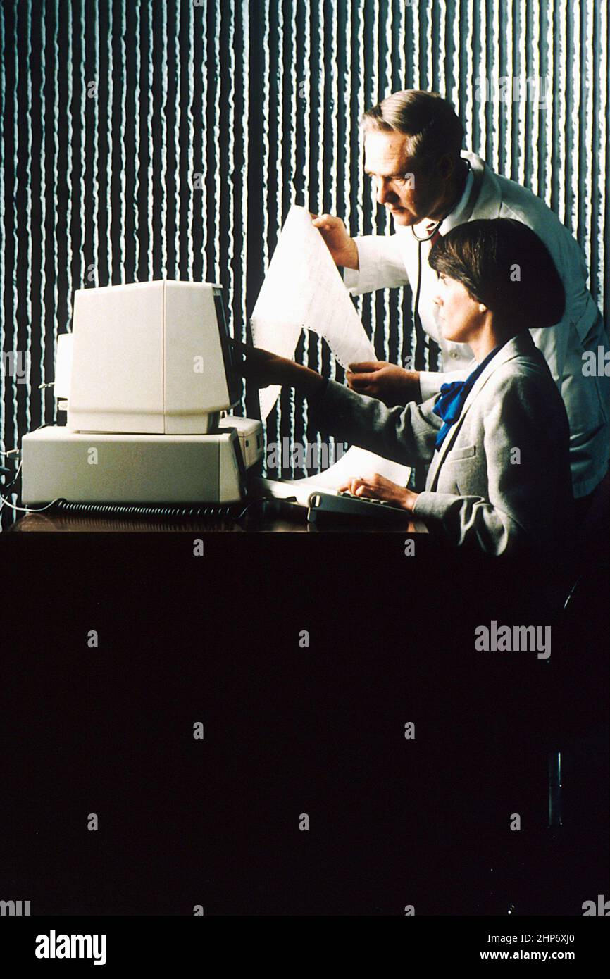 A female librarian seated at a computer working with PDQ, while a male ...