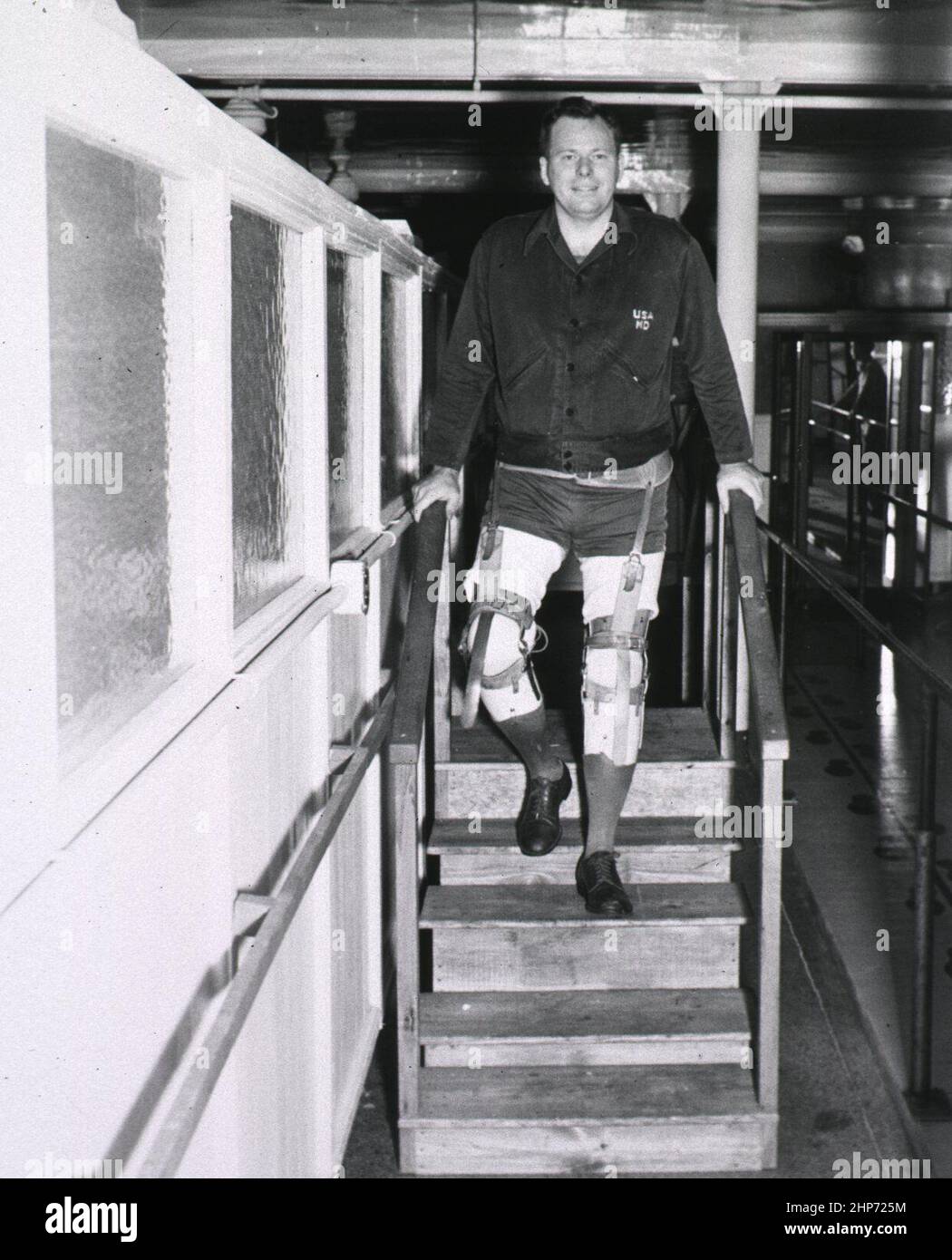 A man with two prosthetic legs holds onto the railing as he walks down ...