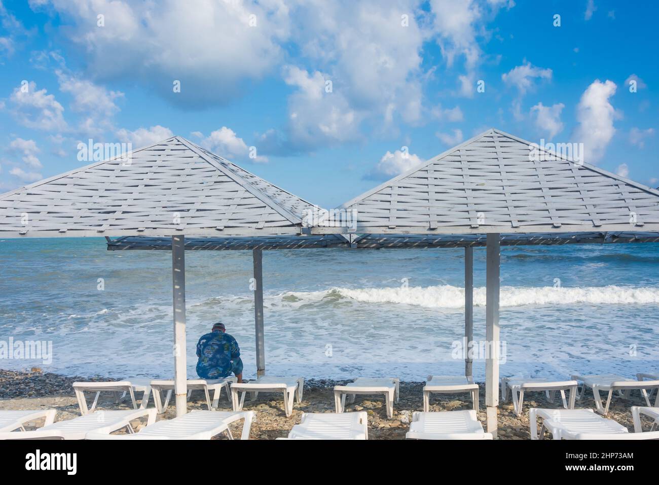Man on an empty sea beach with waves. Large umbrellas and sun loungers ...