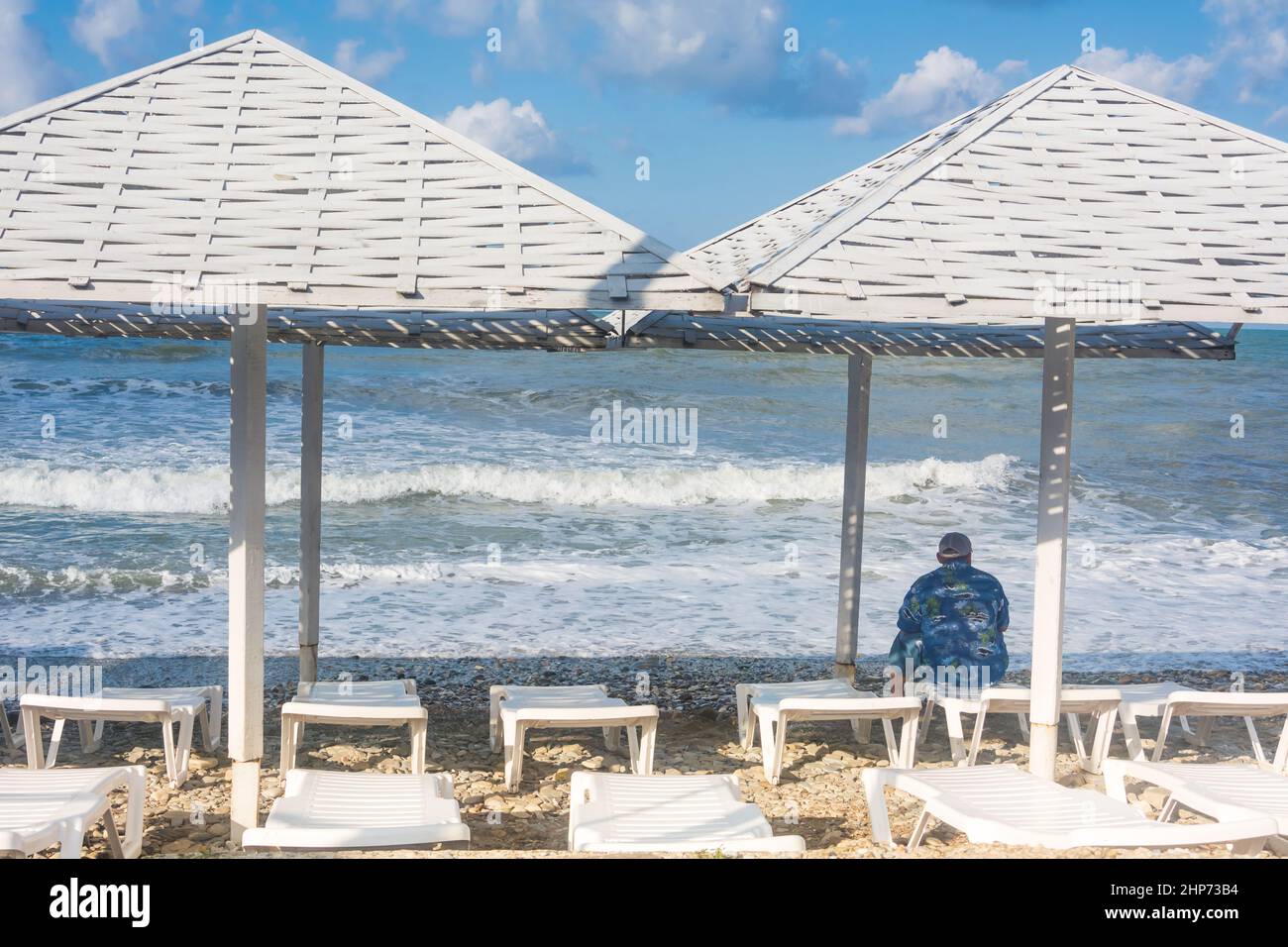 Empty sun loungers under umbrellas on seashore in storm. A lonely man ...