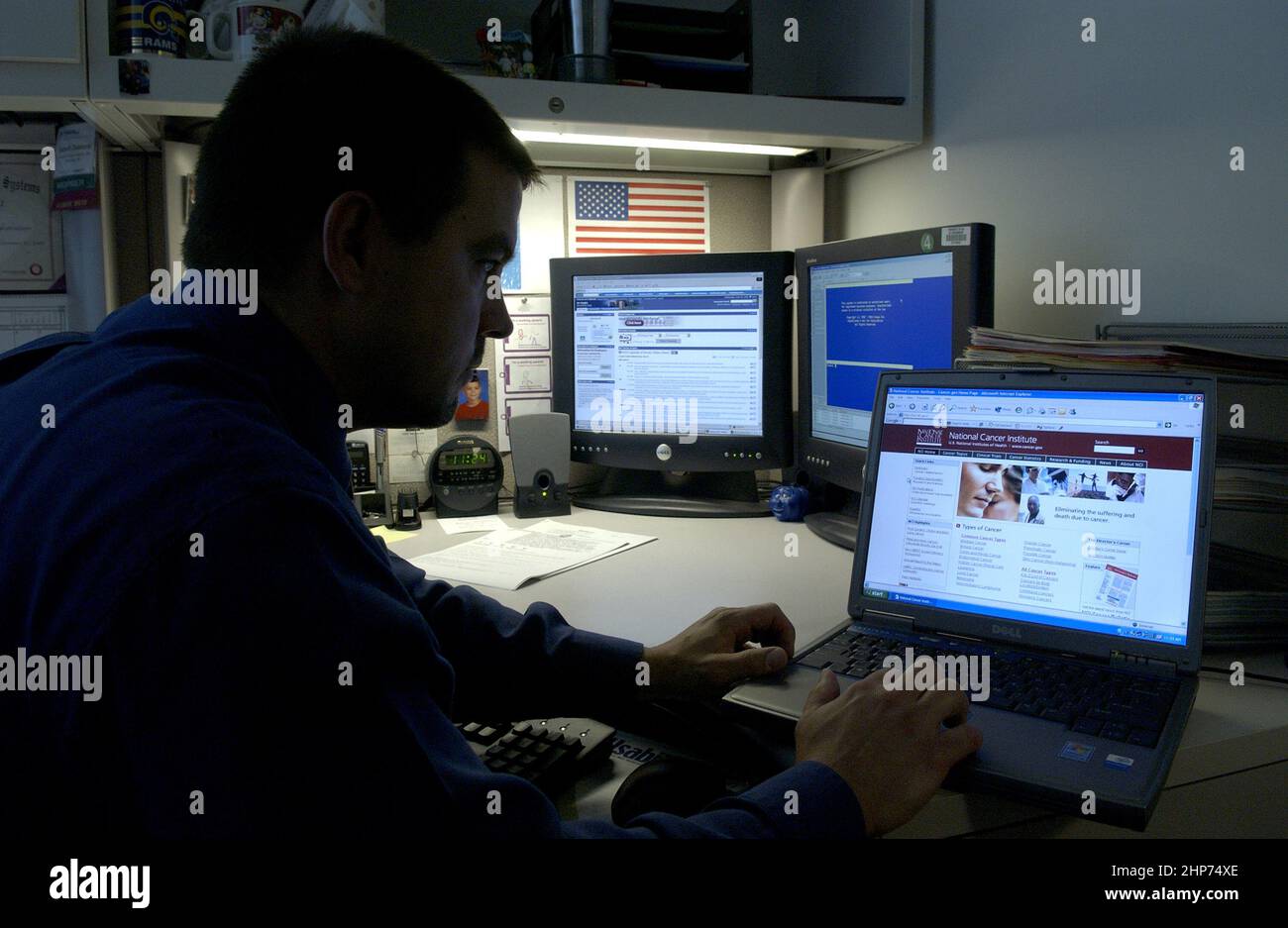A man uses his laptop computer at his desk in a darkened room. A ...