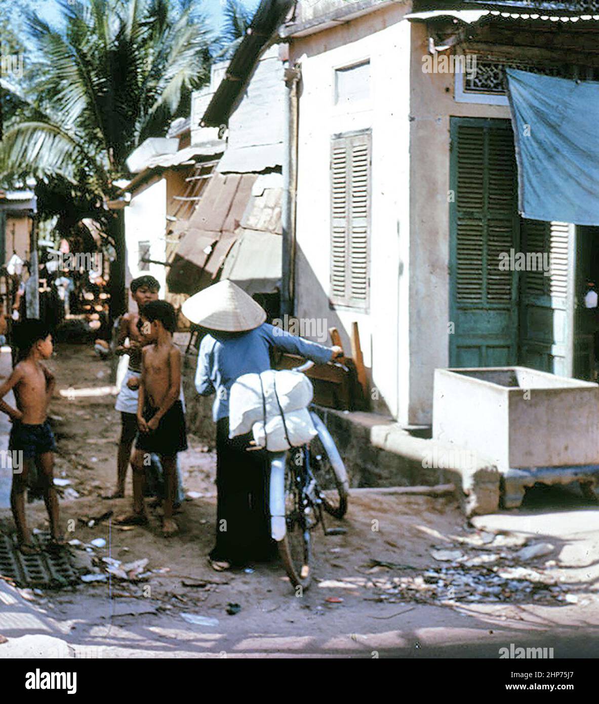 A Vietnamese woman with her bicycle and several children in an alleyway ...