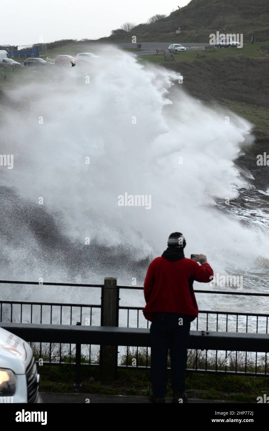The Mumbles .18th Feb. 2022 Waves surge up the cliffs while a passerby ...