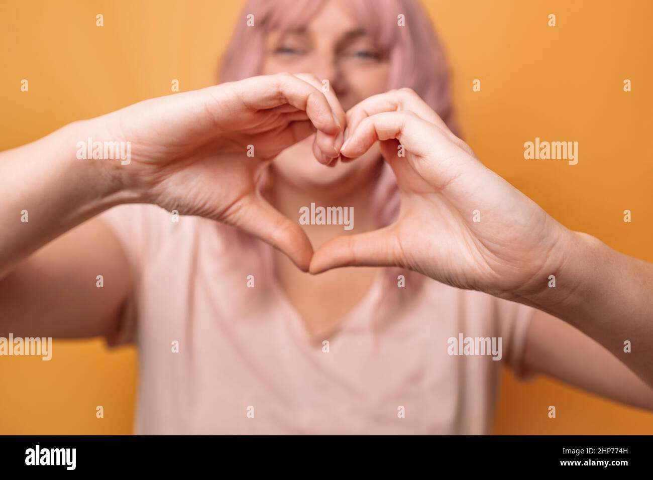 Woman making heart with her hands, love symbol over yellow background ...