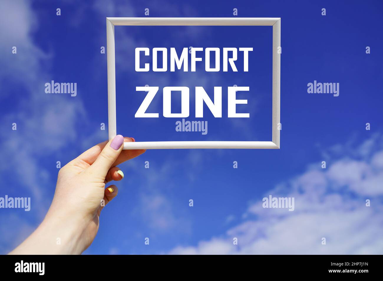 Comfort zone. White frame in a female hand against the blue sky. The ...