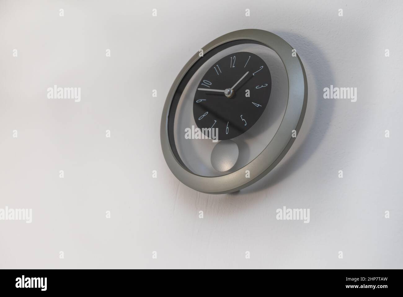 A round wall clock with a pendulum is mounted on a white wall Stock ...