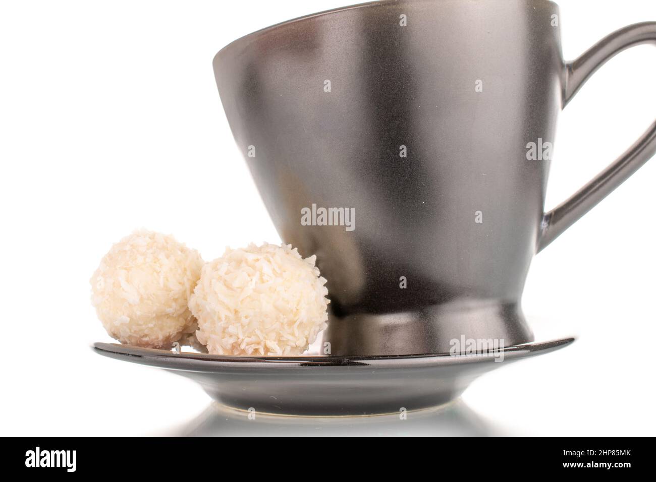 Two sweet coconut candies on a saucer with a black cup, macro, isolated ...