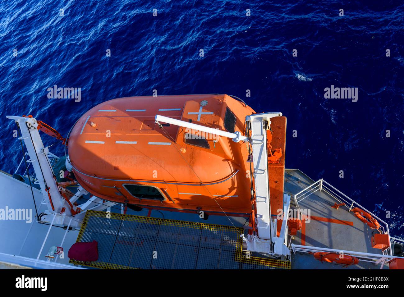 Lowering orange totally enclosed lifeboat to water. Abandon ship drill ...