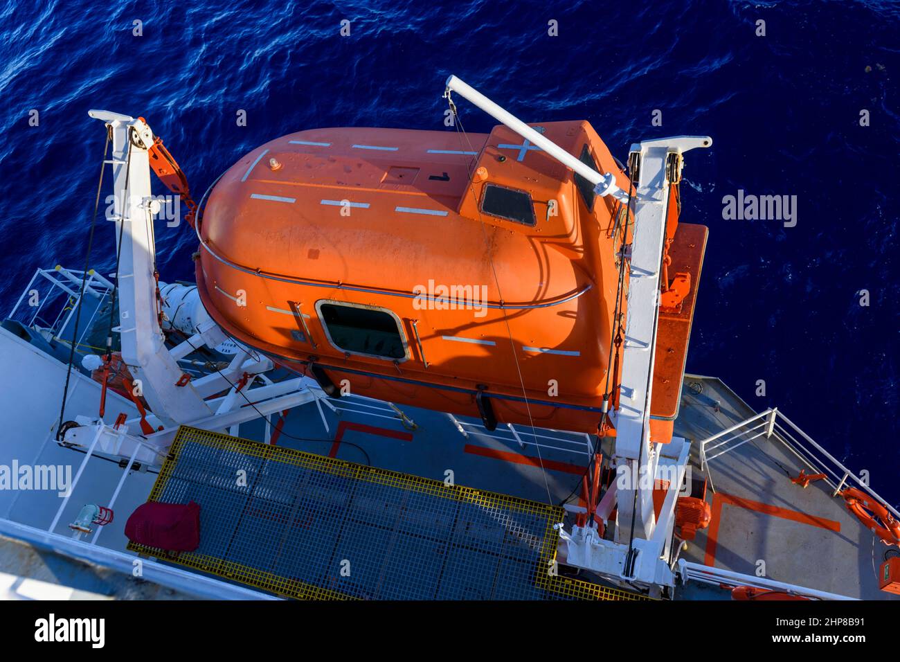 Lowering orange totally enclosed lifeboat to water. Abandon ship drill ...