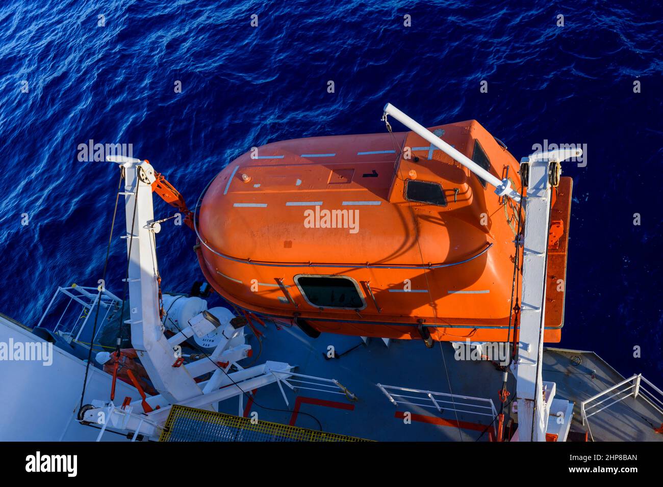 Lowering orange totally enclosed lifeboat to water. Abandon ship drill ...