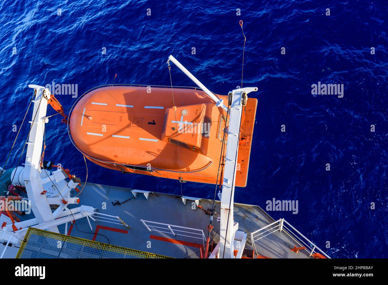 Lowering orange totally enclosed lifeboat to water. Abandon ship drill ...