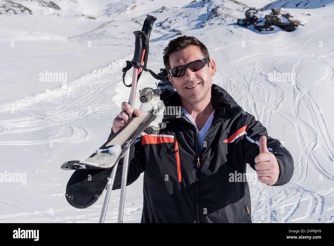 Handsome skier with his skis on his shoulder looking at the camera and ...