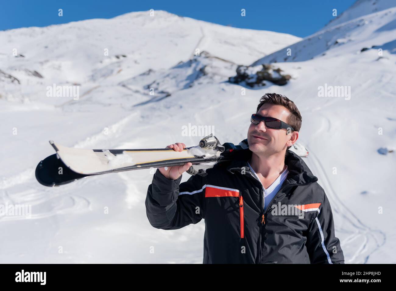 Handsome skier with his skis on his shoulder looking to the side and ...