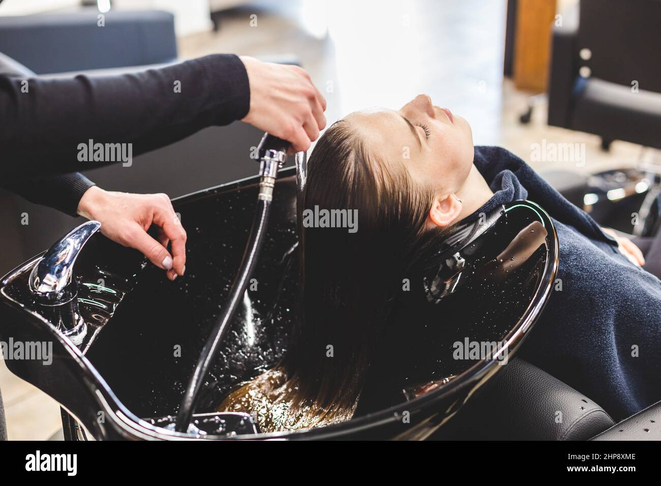 Master woman hairdresser gently washes the girl's hair with shampoo and ...