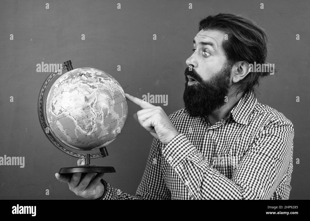 surprised bearded man in checkered shirt looking at geographic globe ...