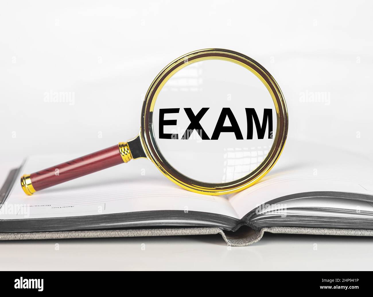 Word EXAM through magnifying glass and book. photo Stock Photo - Alamy