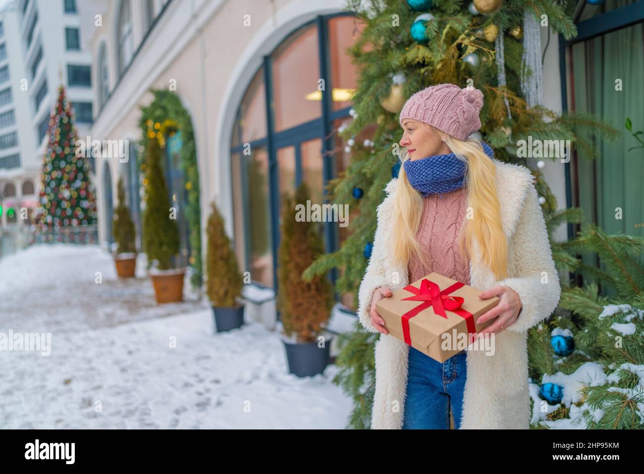 girl with a gift in red jacket and hat standing near a large Christmas ...