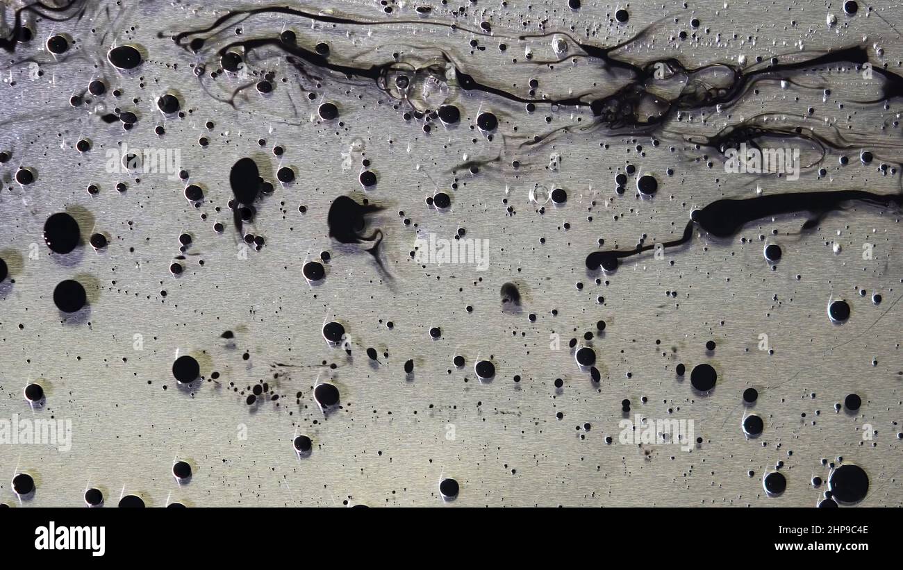 Top view of black ink drops flowing in liquid oil on metallic, grey ...