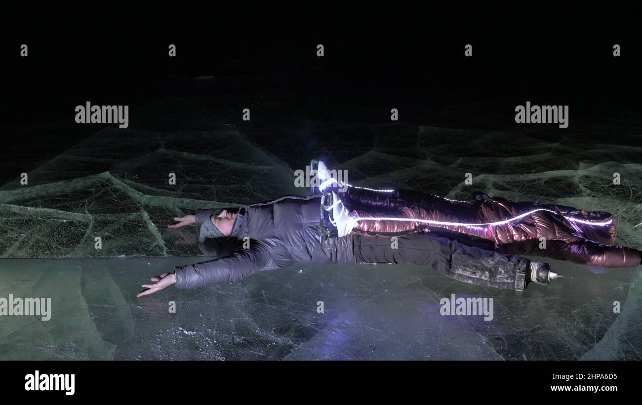 Young loving couple skating at ice rink at night. Man and woman kiss ...