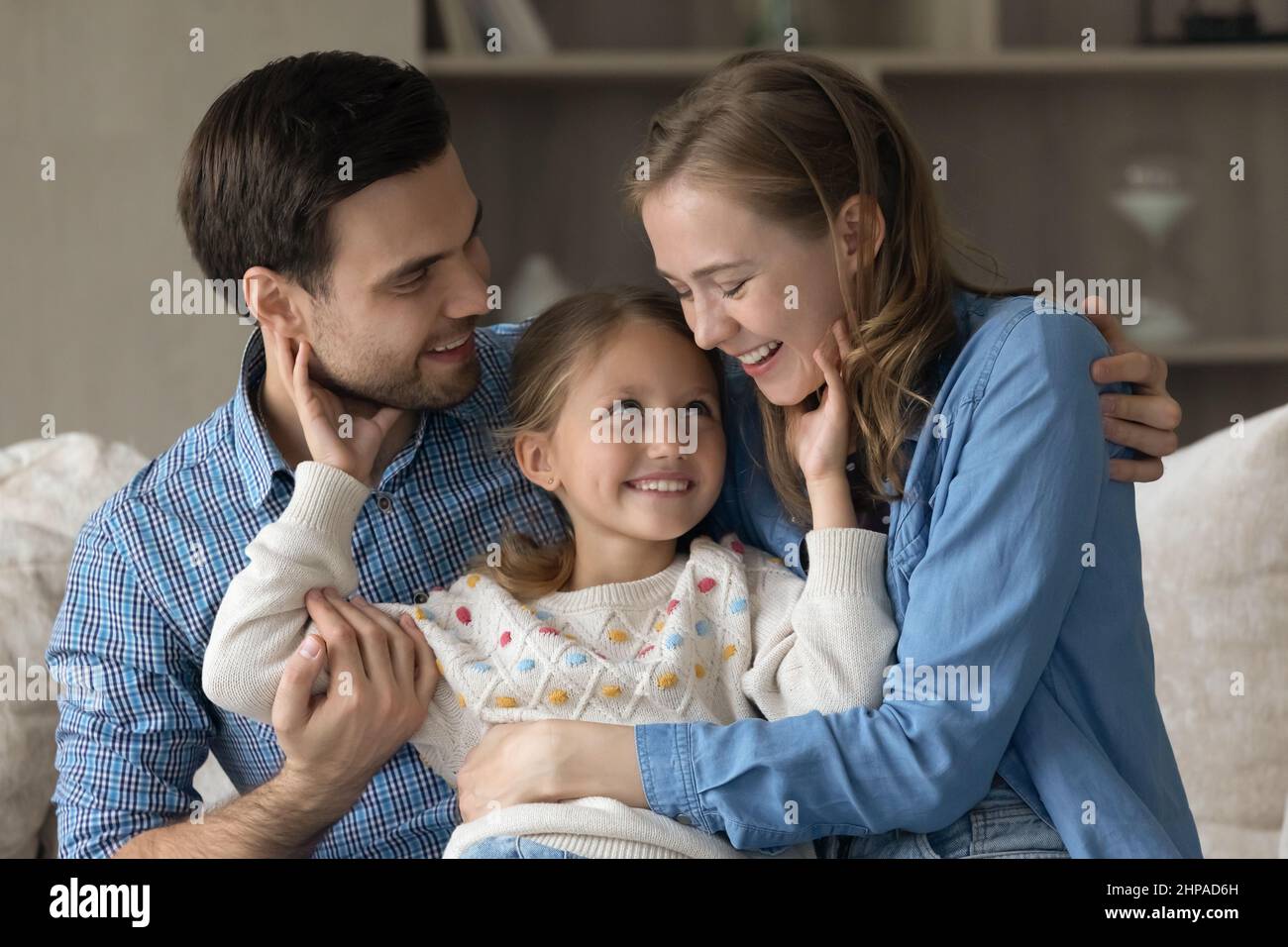 Cheerful family couple of millennial parents cuddling cute daughter ...