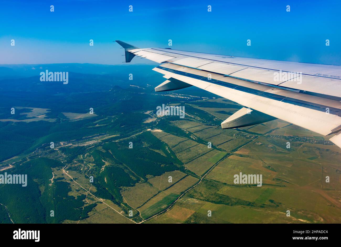View of airplane wing, blue skies and green land during landing. Airplane window view. Earth and ...