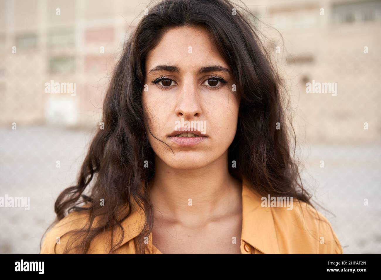 Confident young woman with dark eyes looking at camera with serious ...