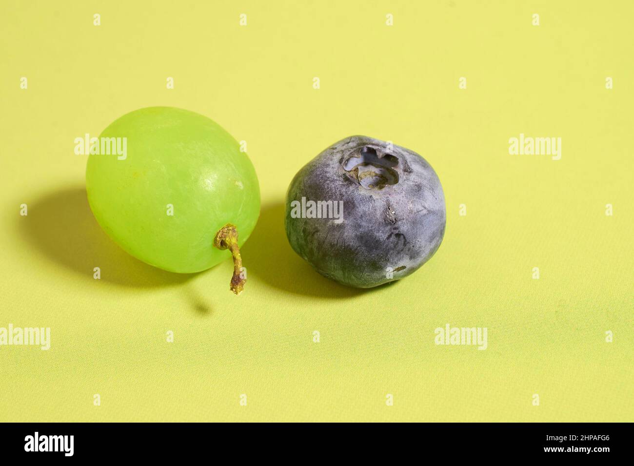 Ripe berries of green grapes and blueberries on a colored background ...