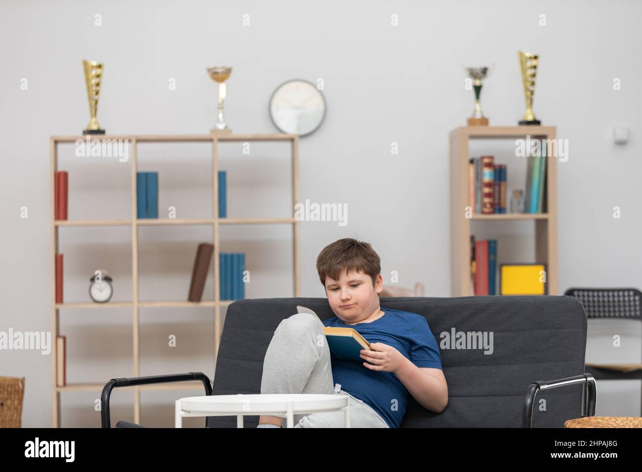 A young boy is sitting at home on the sofa reading a book Stock Photo ...