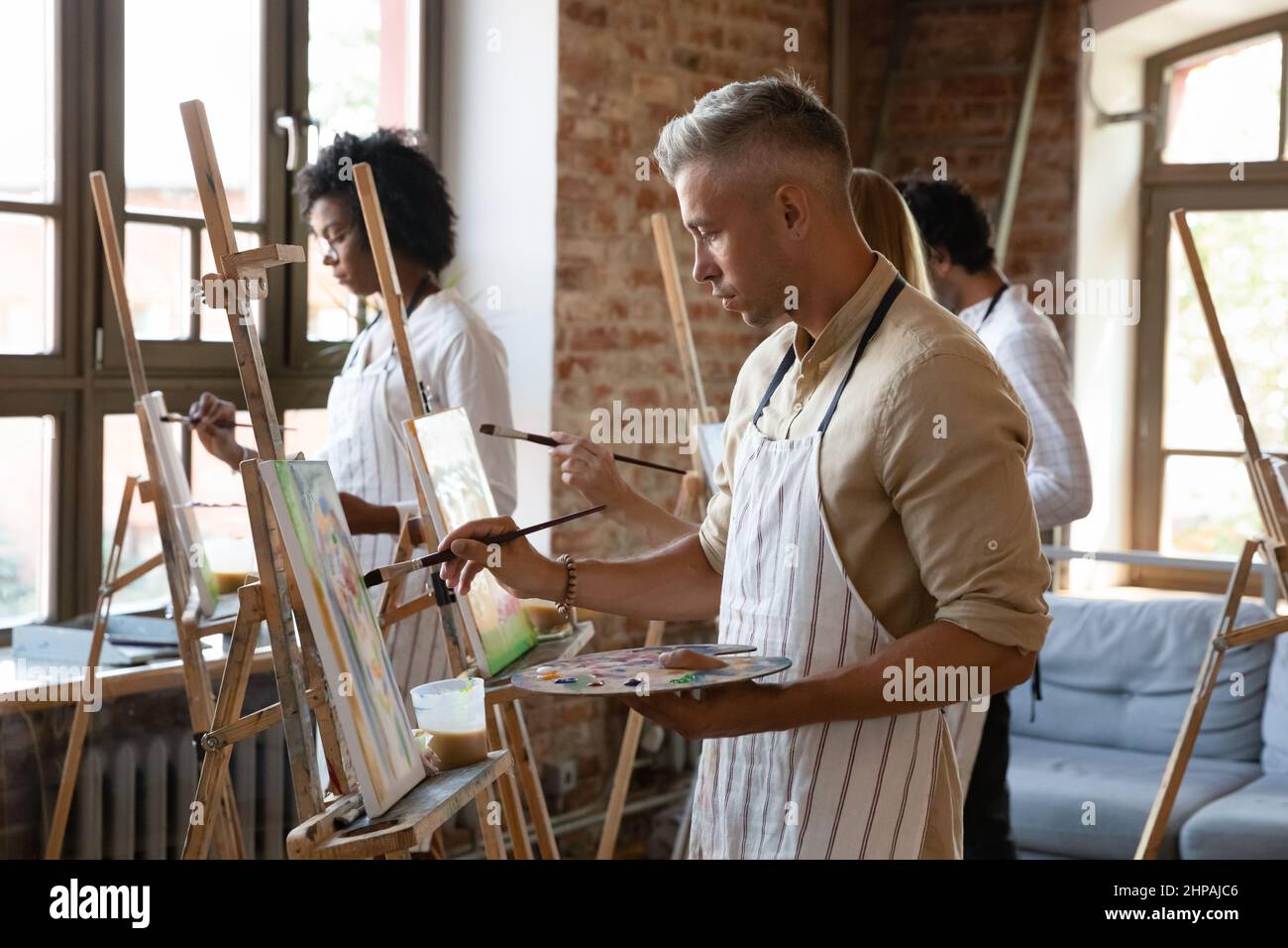 Concentrated young handsome man drawing on easel in studio Stock Photo ...