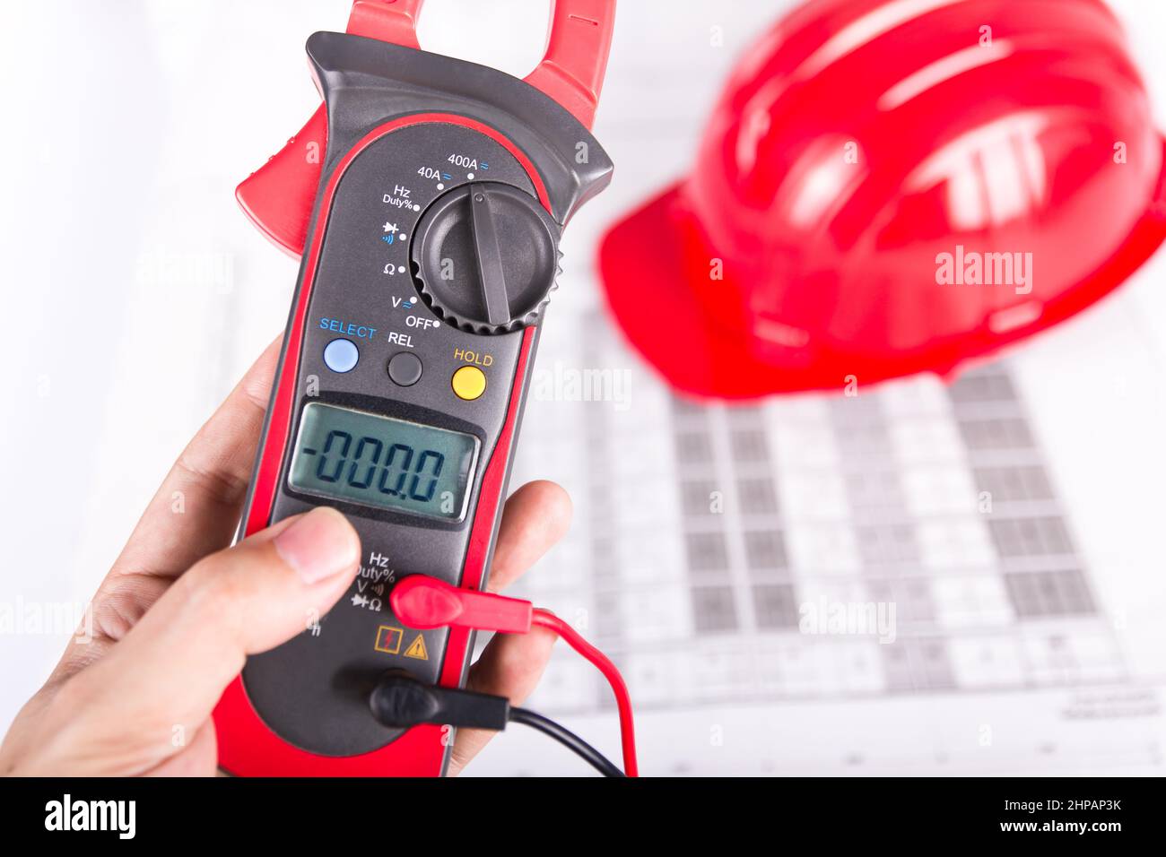 Hand of technician holding digital clamp multimeter over blueprint and ...