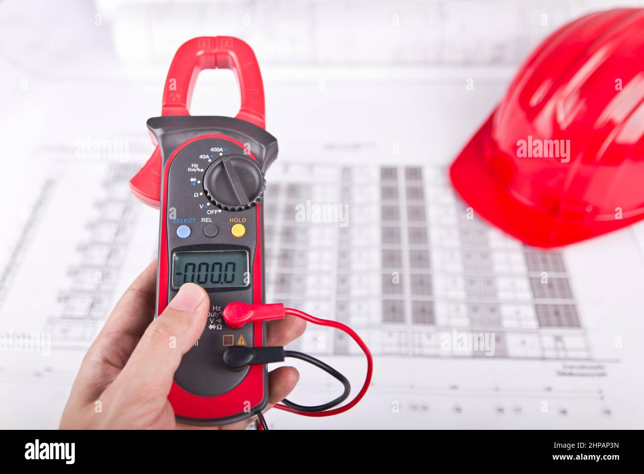 Hand of technician holding digital clamp multimeter over blueprint and ...