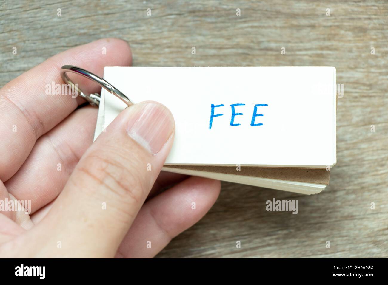 Man hold the flash card with handwriting word fee on wood background ...