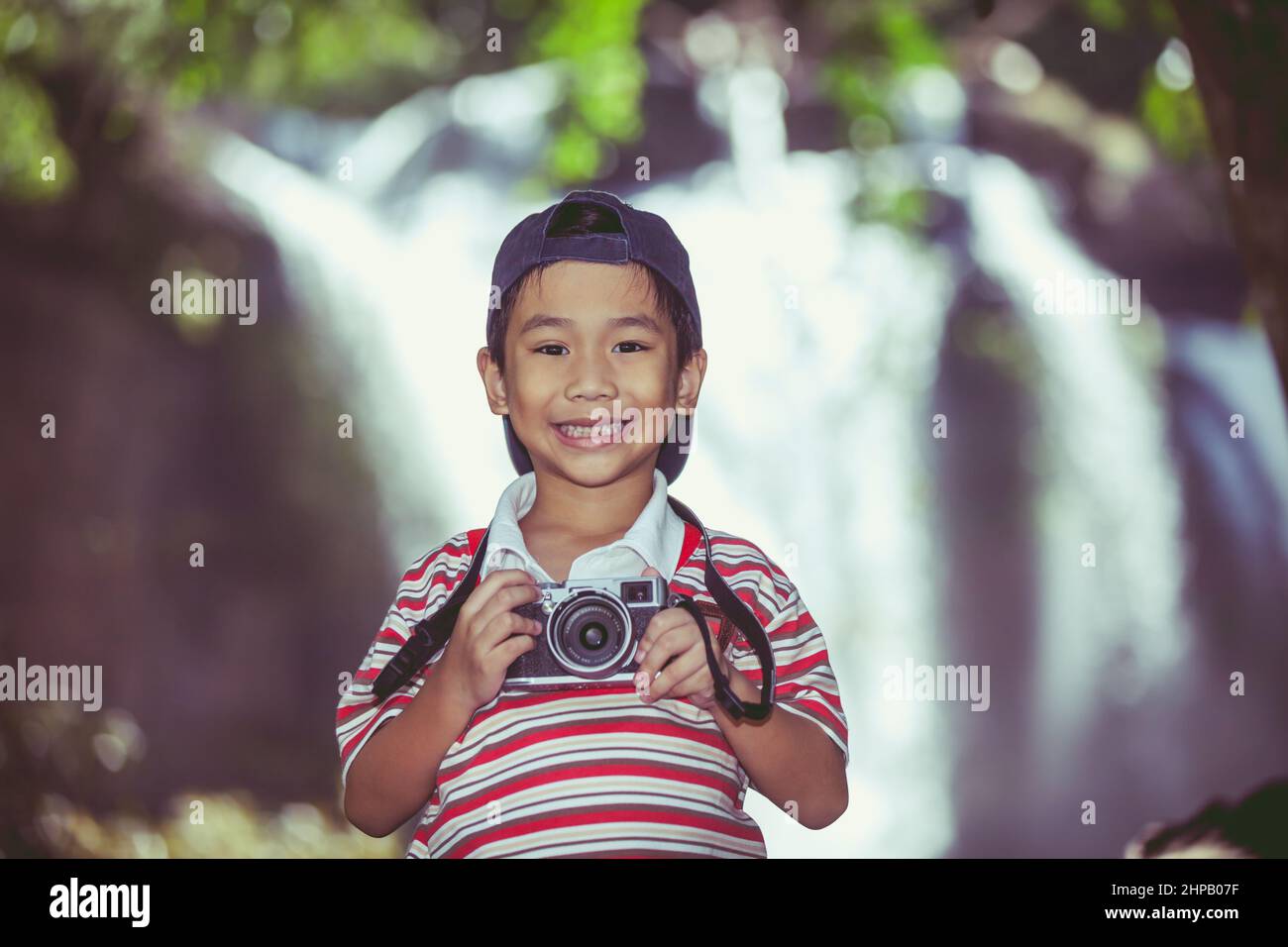 Asian child smiling and holding professional digital camera on blurred ...
