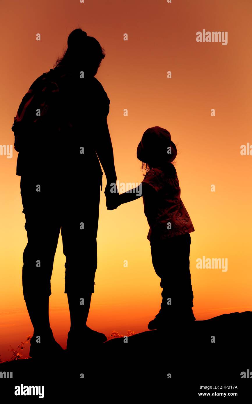 Silhouette back view of mother and daughter clasping hand together at ...