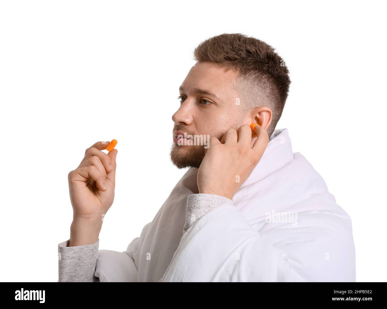 Young man with blanket putting ear plugs on white background Stock ...