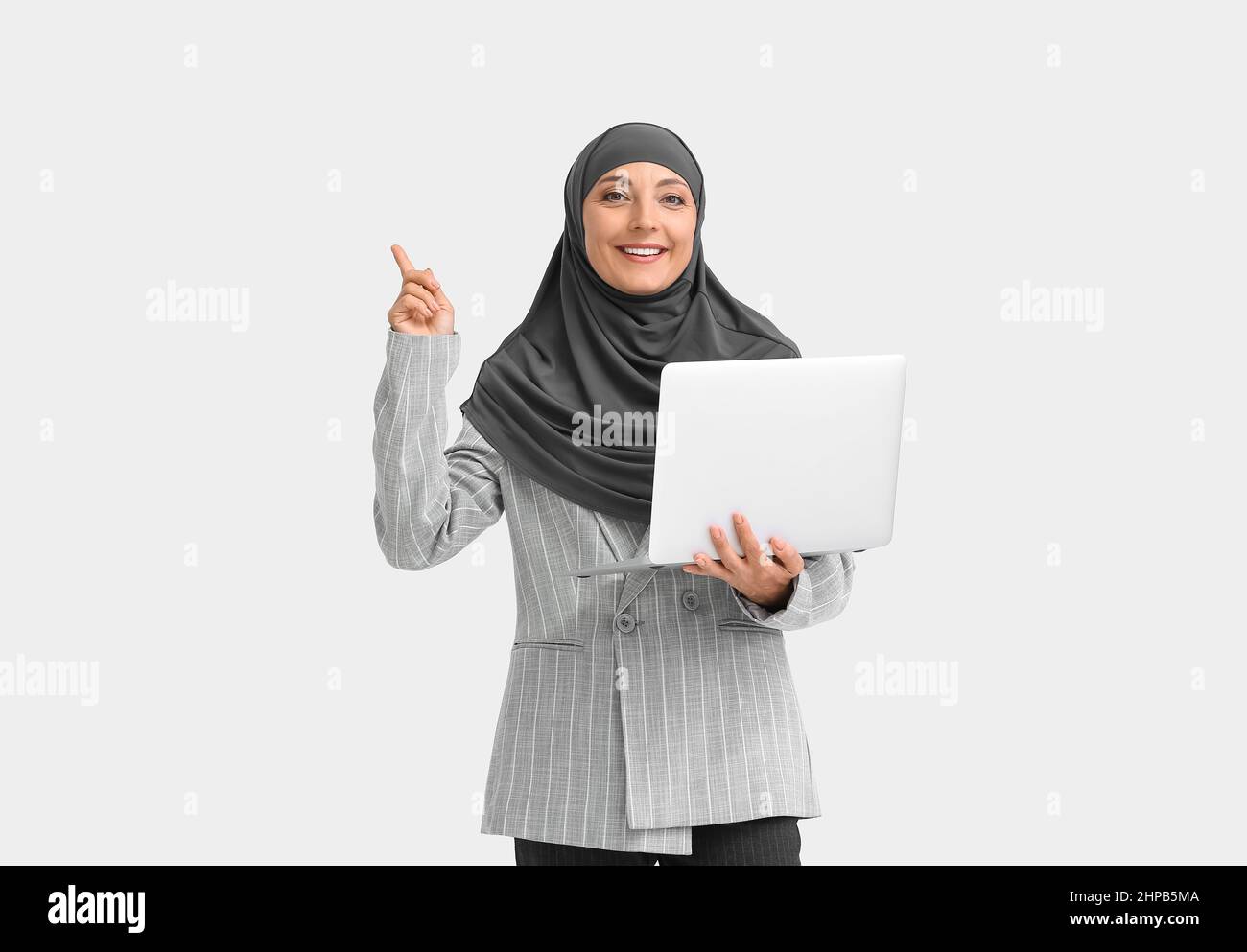 Muslim secretary with laptop pointing at something on light background ...