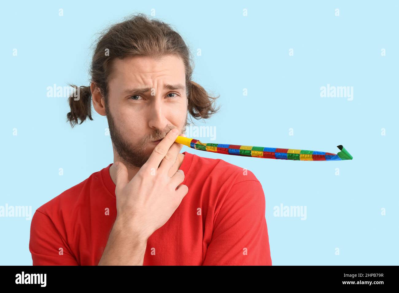 Funny young man with party whistle on blue background. April fools' day ...