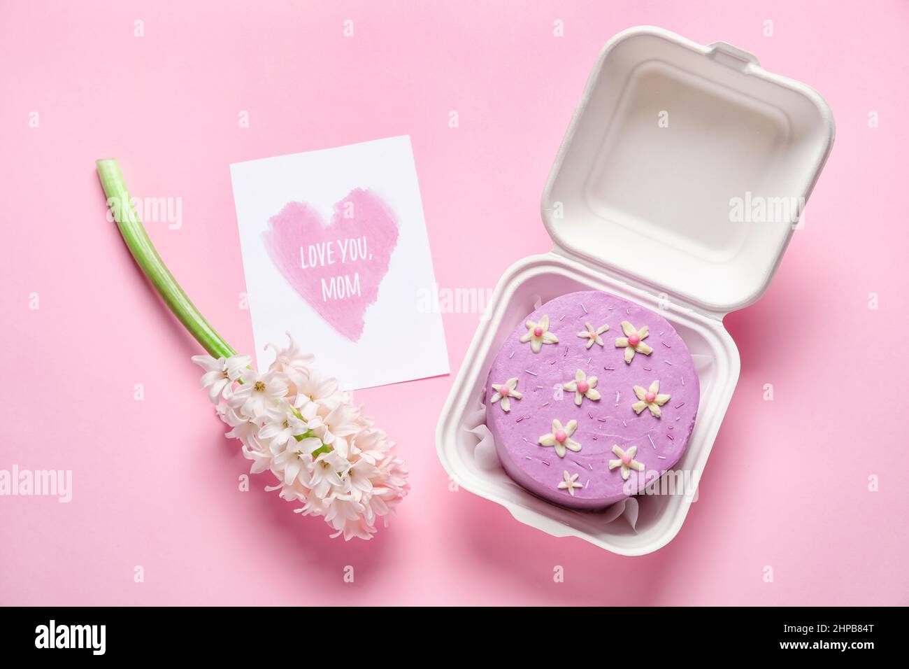 Plastic lunch box with tasty bento cake, greeting card and flowers on ...