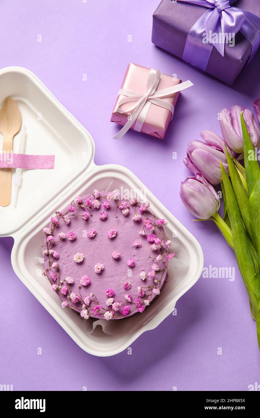 Plastic lunch box with tasty bento cake and flowers on purple ...
