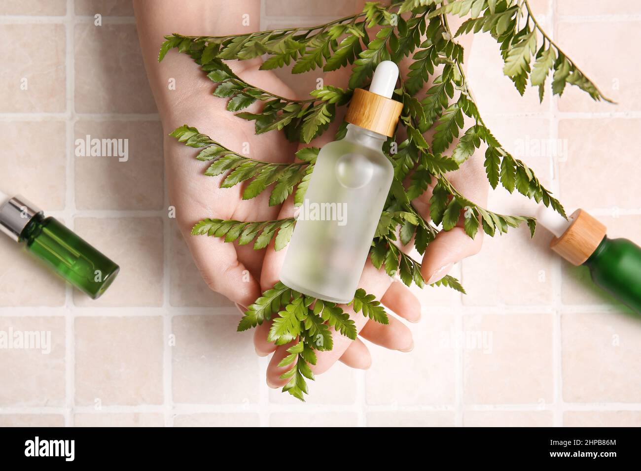 Female hands with bottle of serum on light tile background Stock Photo ...
