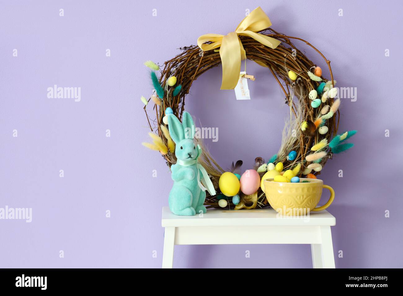 Beautiful Easter wreath, rabbit and cup on stepladder stool near color ...